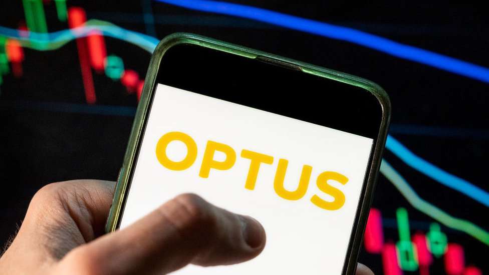 A person holding a mobile phone with the Optus logo showing on the screen.